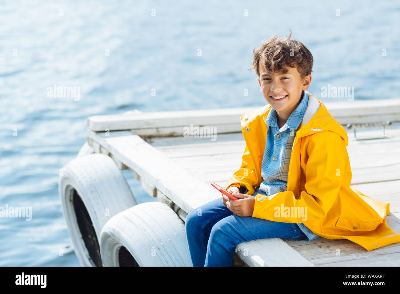 Cheerful dark-eyed boy feeling happy while sitting near river Stock ...