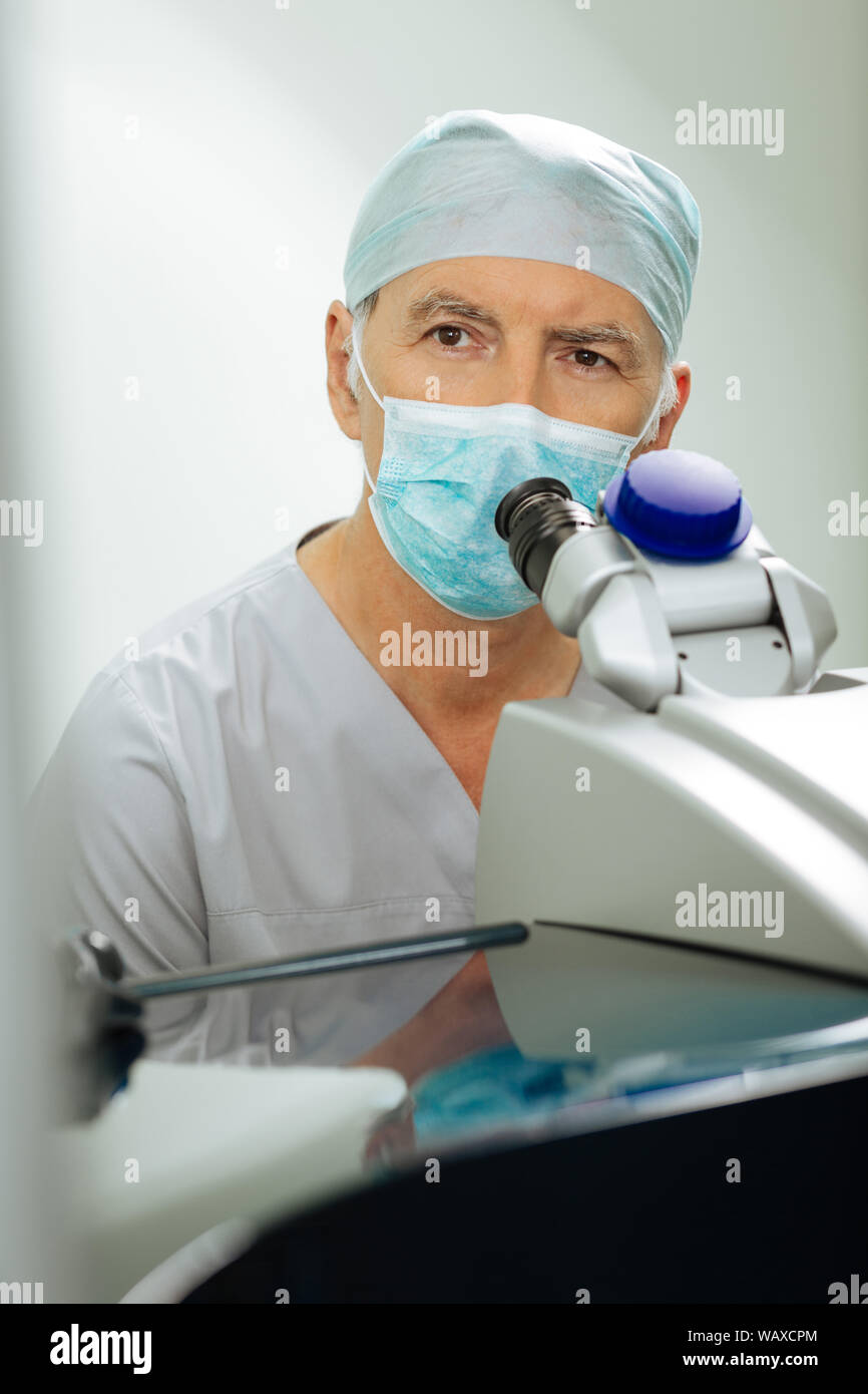 Smart male optometrist sitting at the microscope Stock Photo - Alamy
