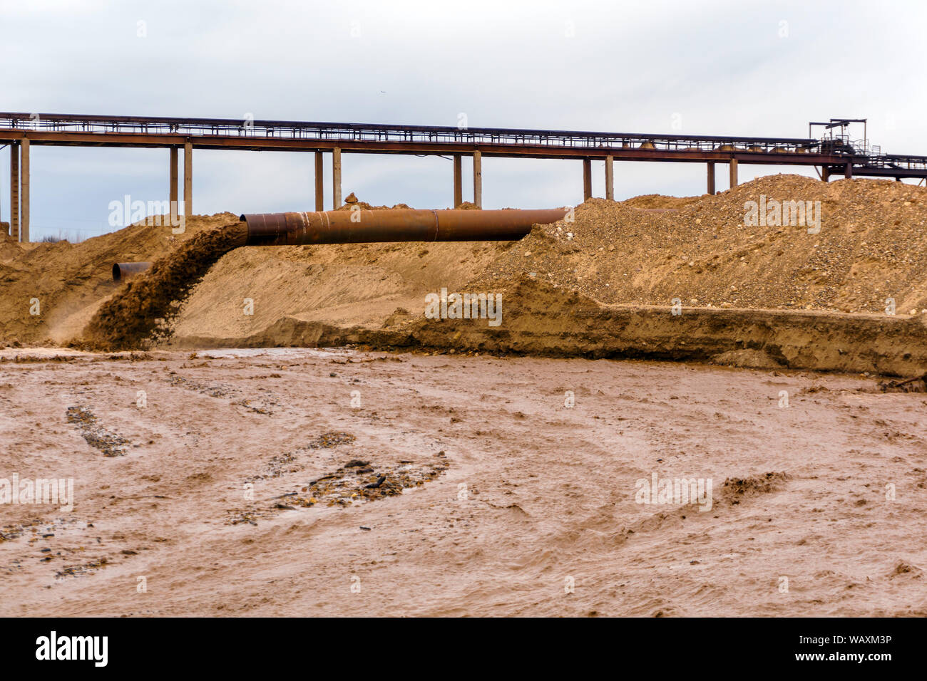 rusty pipe on the river bank, from which sewage flows, dirty sand ...