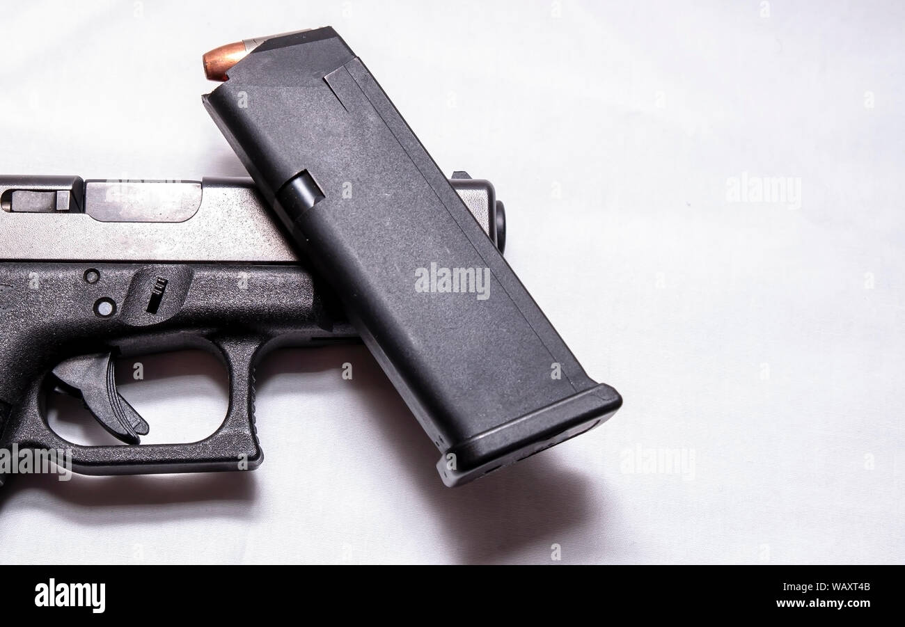 A loaded 9mm pistol magazine on top of a black 9mm pistol on a white ...