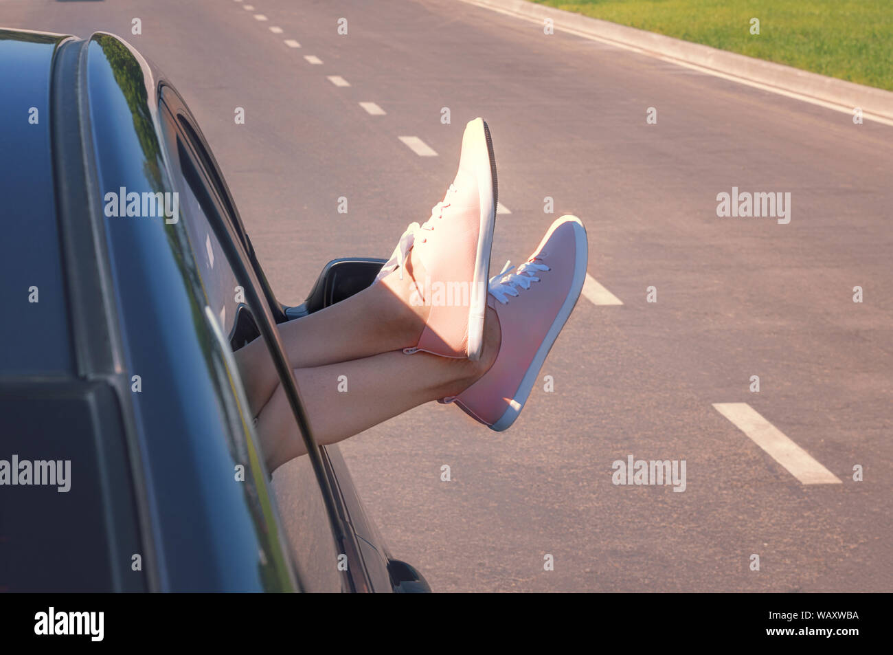 Women's feet in the car window on the road background. The concept of ...