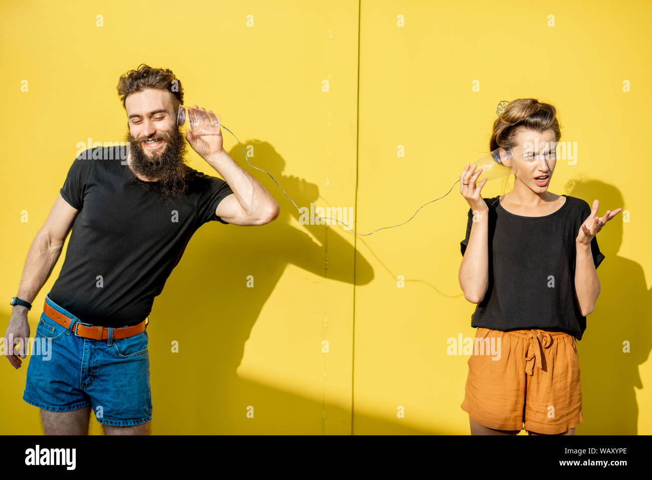 Man and woman talking with string phone made of cups on the yellow ...