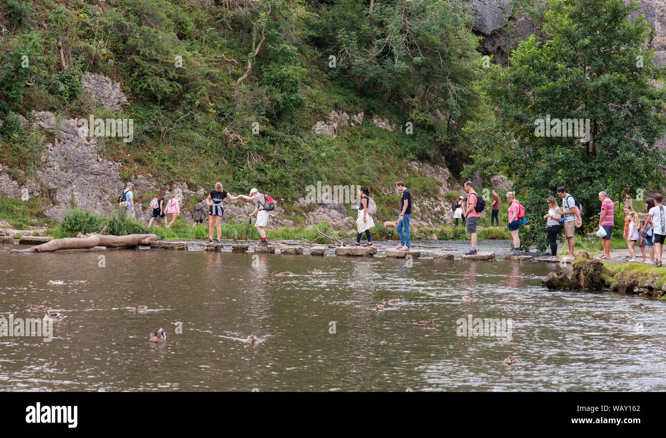 elderly man being helped across the stepping stones across the river ...