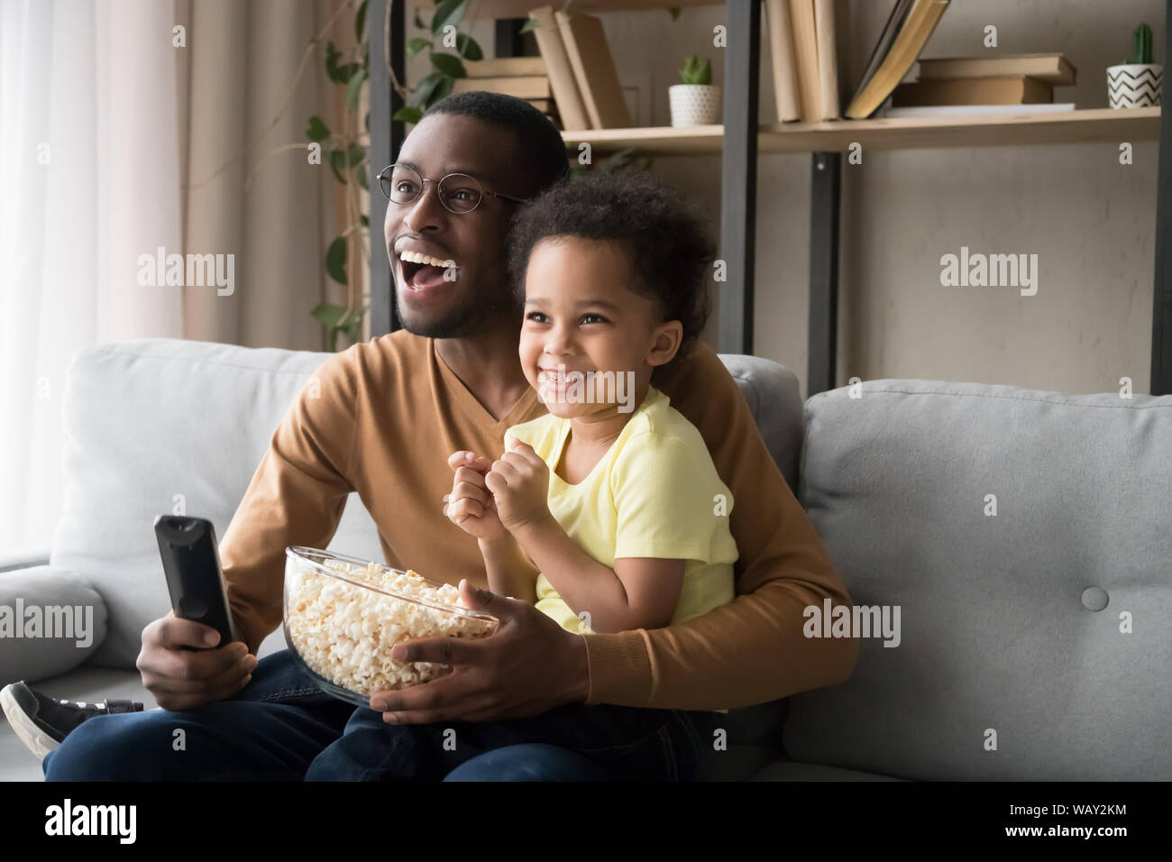 Happy African American father with son watching tv, eating popcorn ...