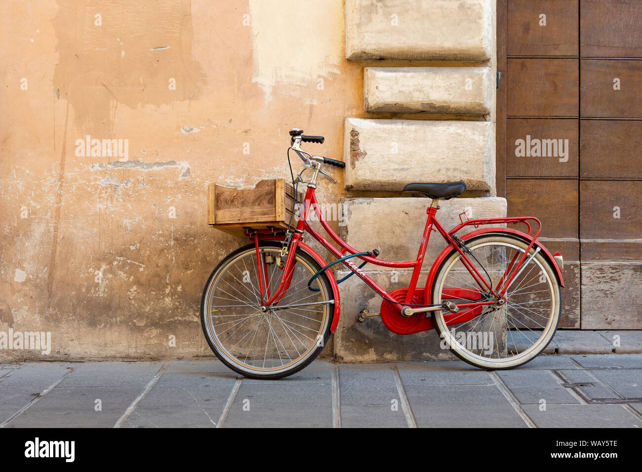 Red classic model women's bicycle with a lock parked against the wall ...