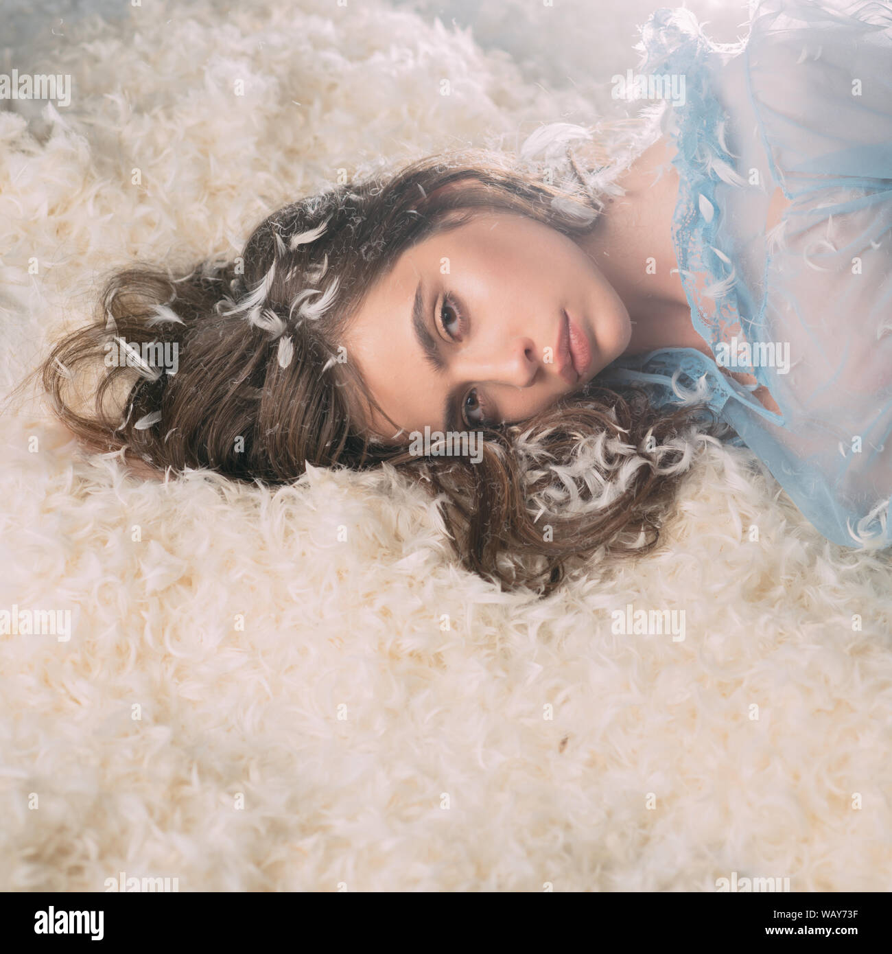 Girl on calm face lay on bed covered with feathers and fluff. Woman ...