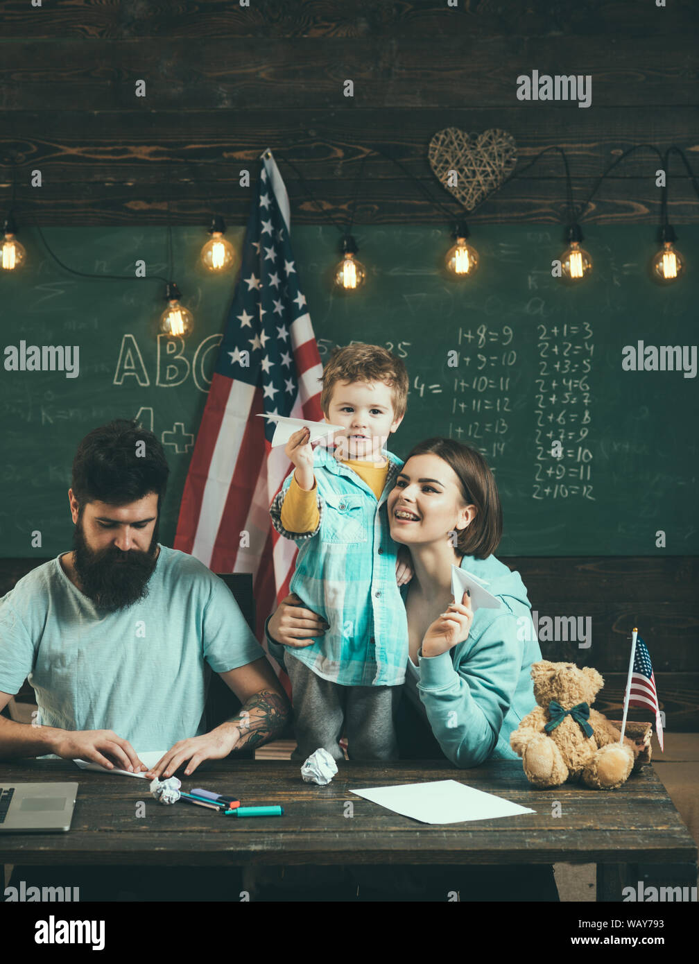 American family at desk with son making paper planes. Parents teaching ...