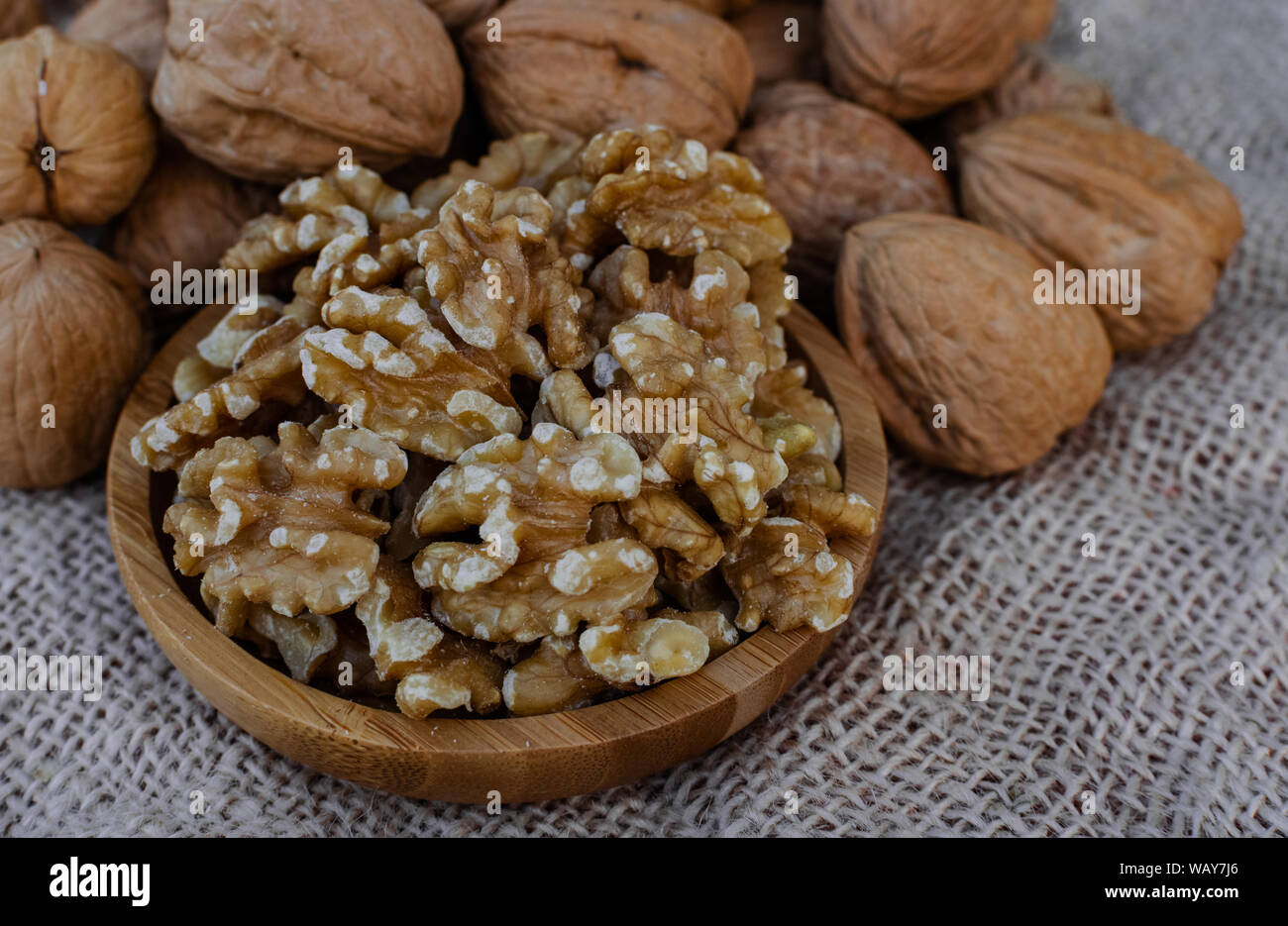 Walnuts in wooden round bowl, and walnuts with shell on sack surface ...