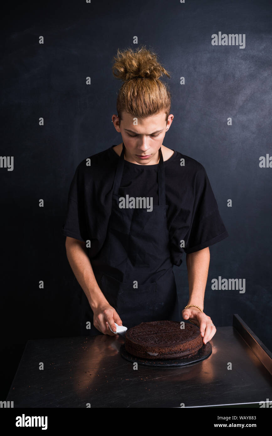Young chef with curvy hair cutting cake in two pieces Stock Photo - Alamy