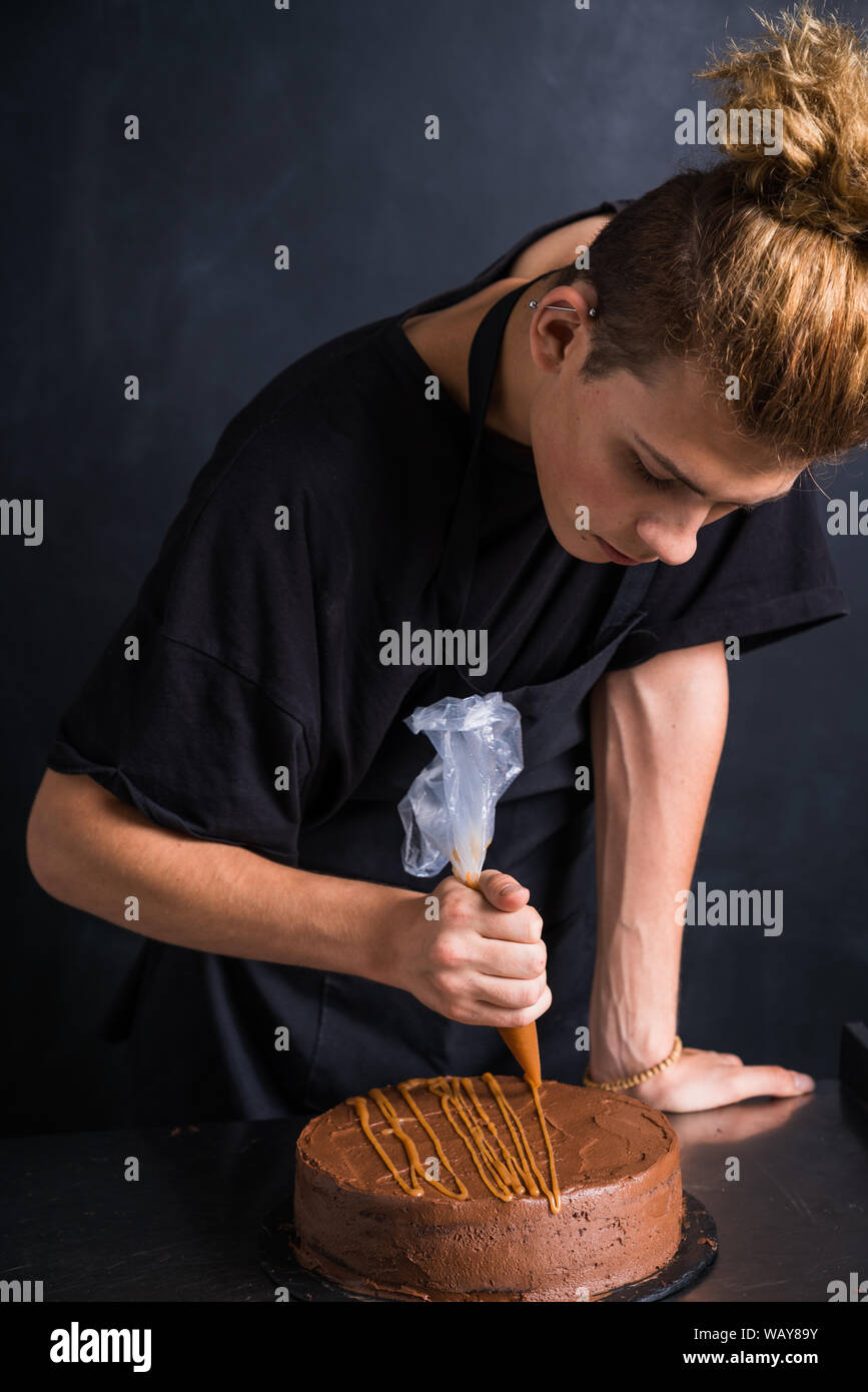 Men decorating chocolate cake with caramel standing in front of black ...