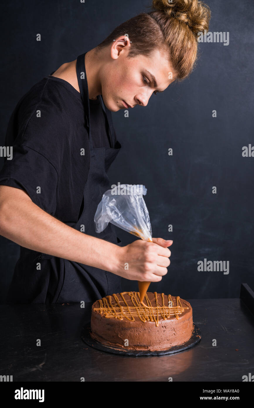 Men decorating chocolate cake with caramel standing in front of black ...