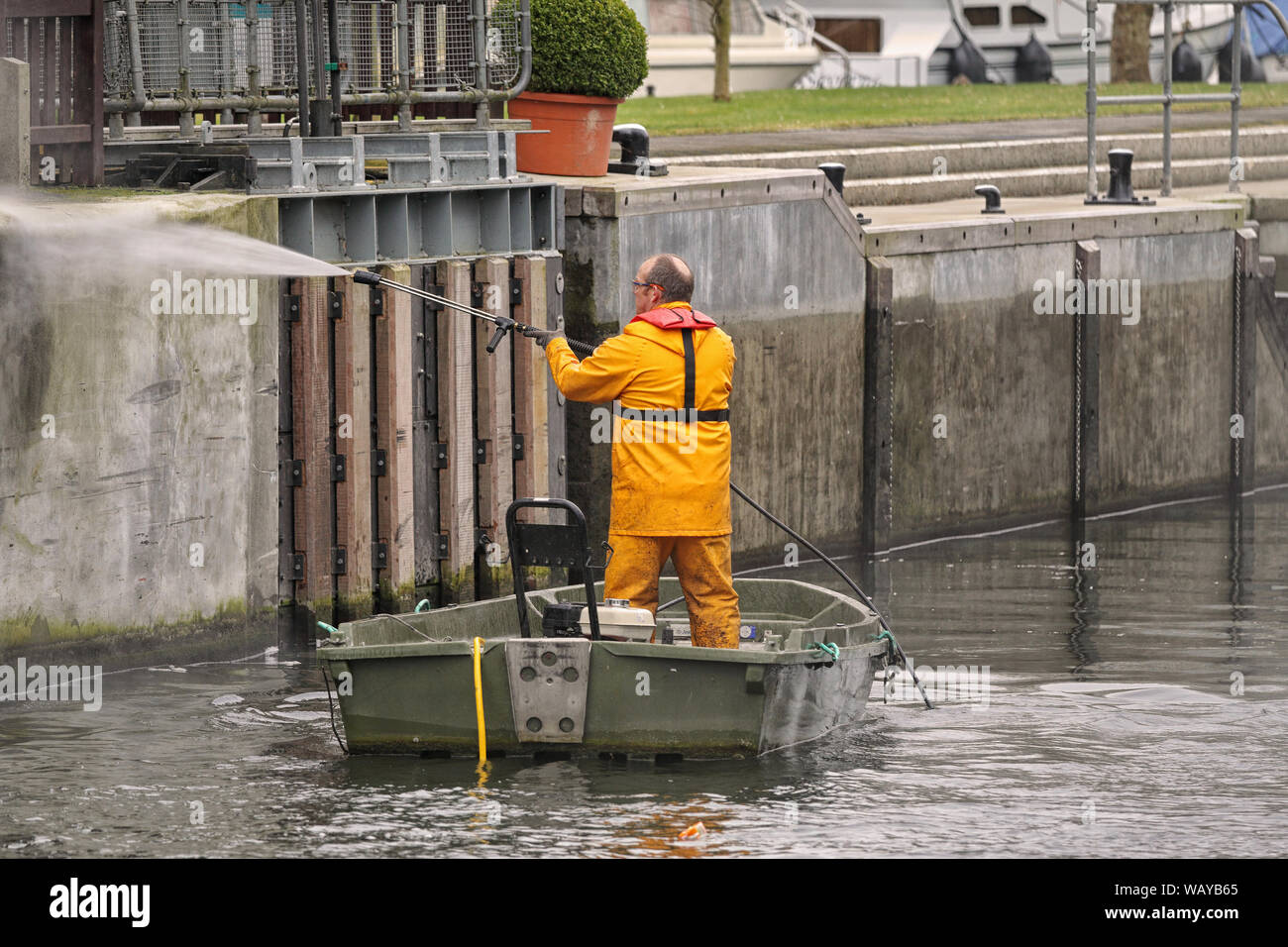 Workman in bright yellow overalls cleaning the walls of a river lock on ...