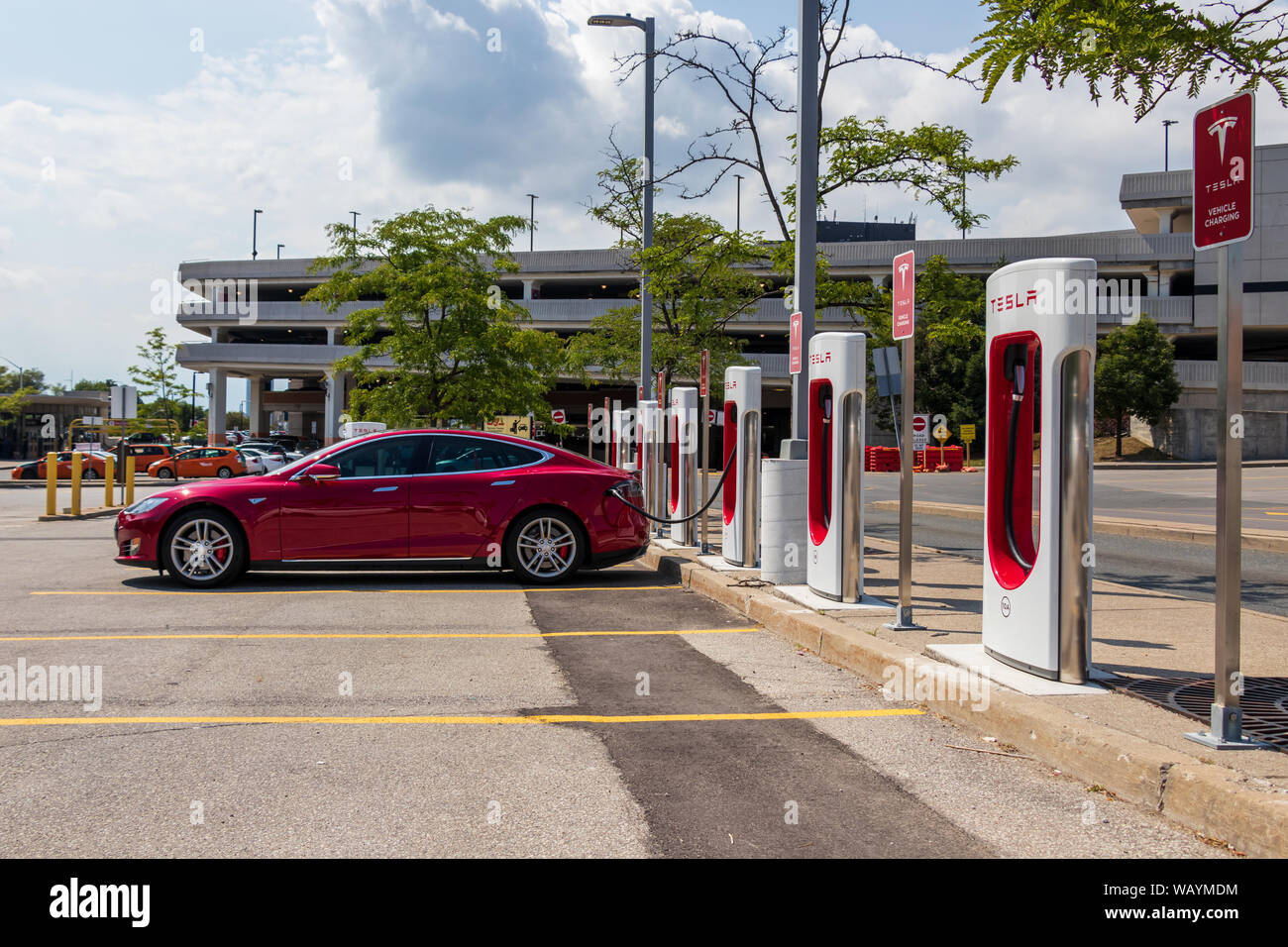 Side-view of red Tesla Model S plugged-in at Tesla Supercharger Station ...