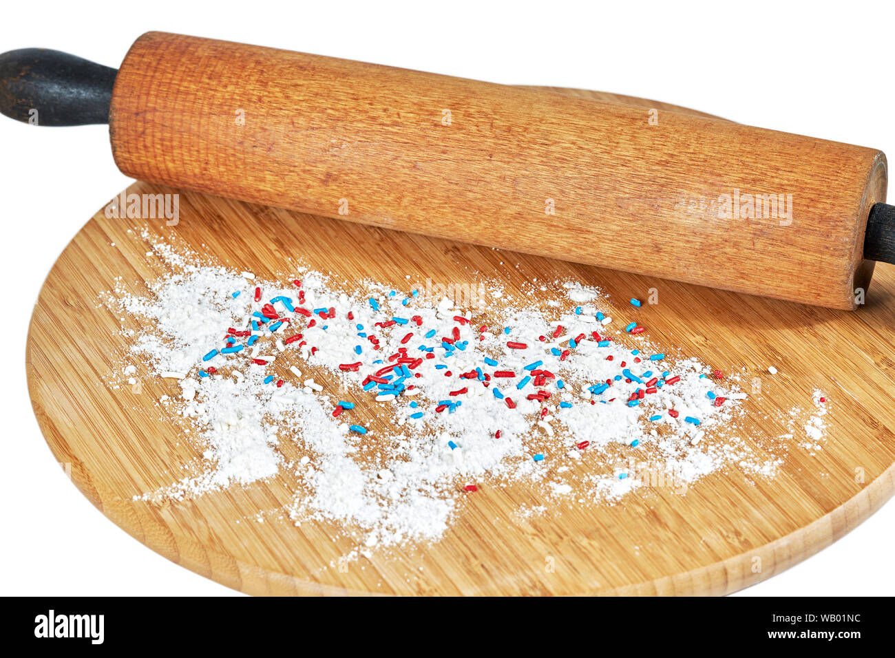 A wooden rolling pin on a bamboo cutting board with white flour and ...