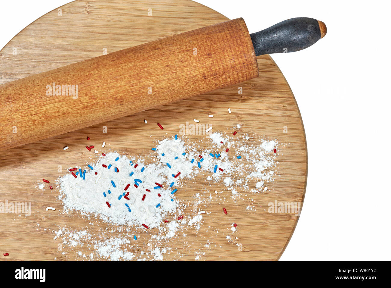A wooden rolling pin on a bamboo cutting board with white flour and red ...