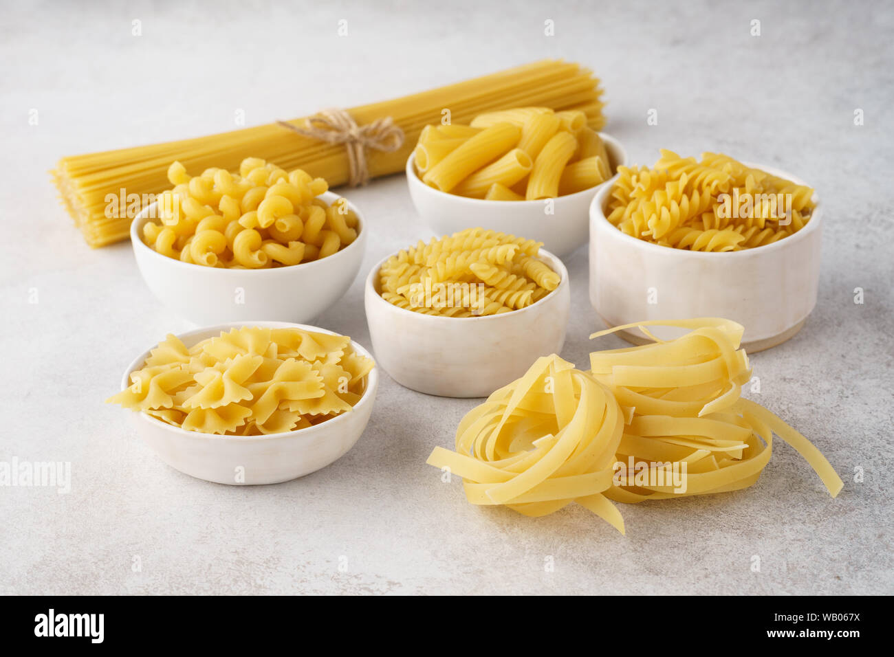 Various types of dry pasta in bowls on light gray background ...