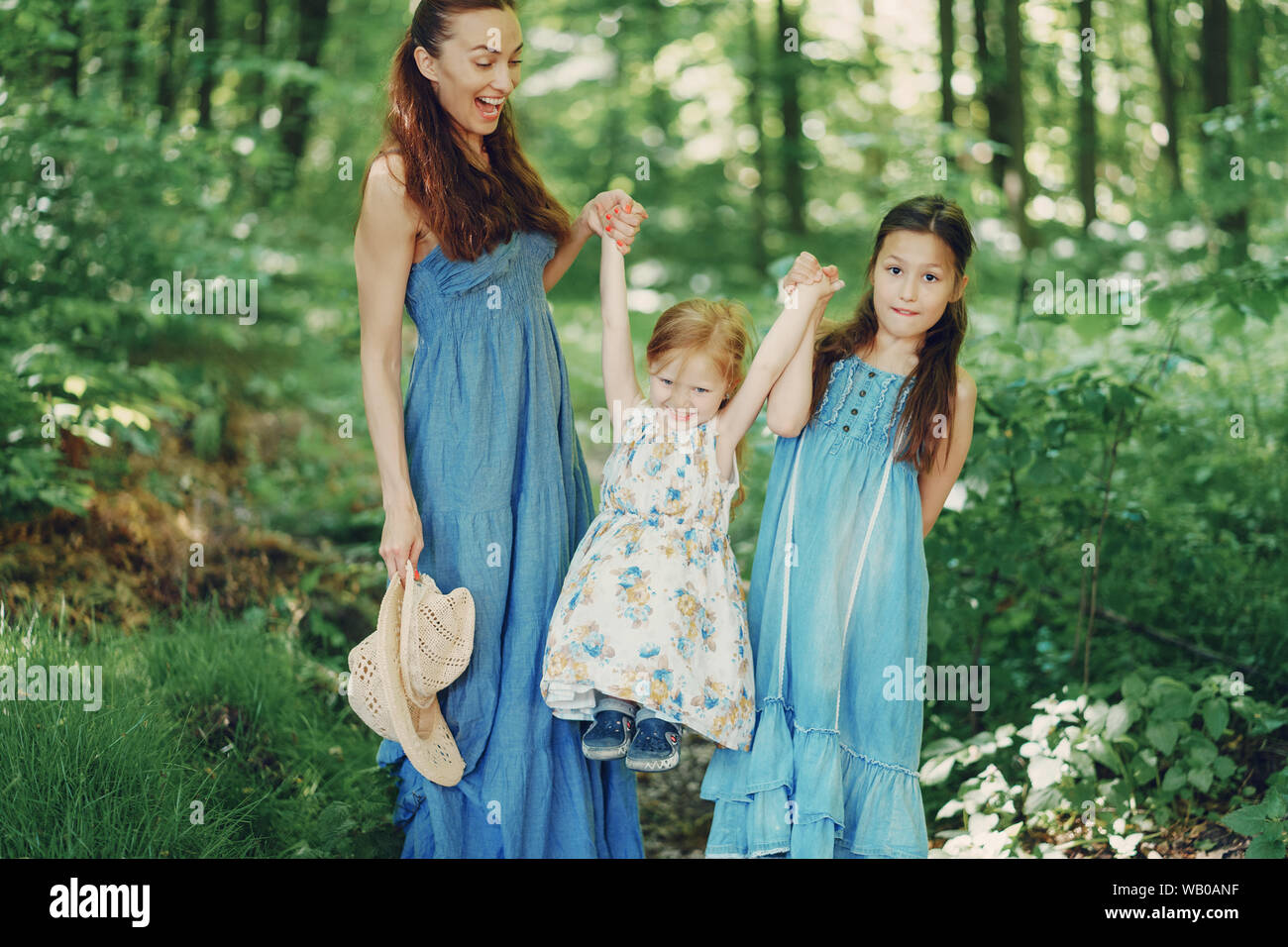 beautiful long-haired mother in a long blue dress in sunny summer ...
