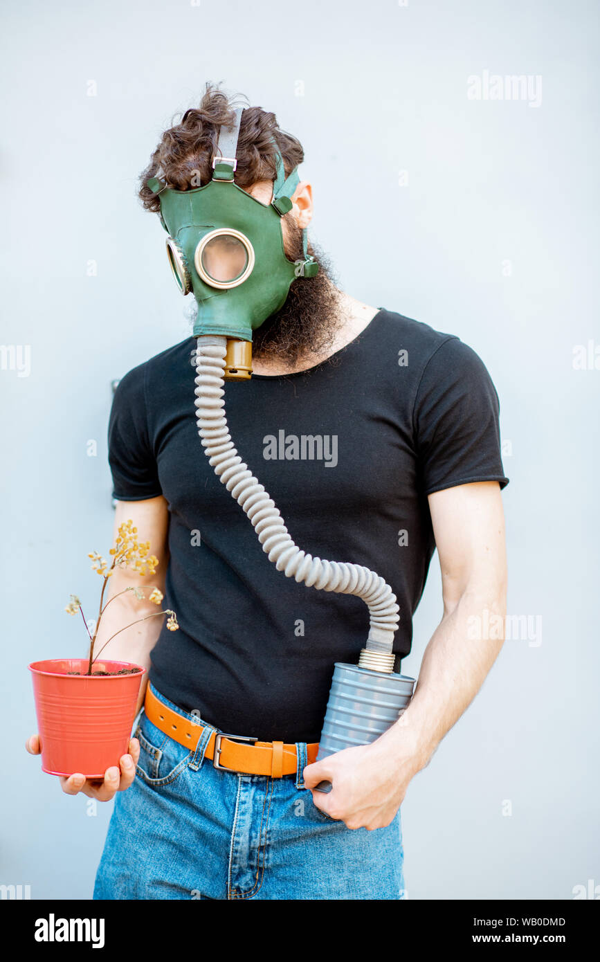 Portrait of a sad man with gas mask and dried flowerpot on the grey ...