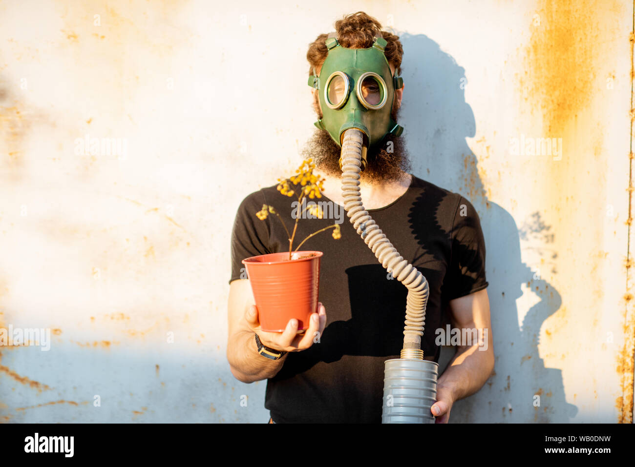 Portrait of a sad man with gas mask holding dried flowerpot on the grey ...