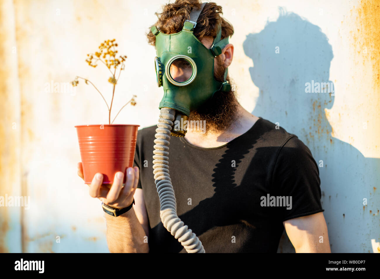 Portrait of a sad man with gas mask holding dried flowerpot on the grey ...