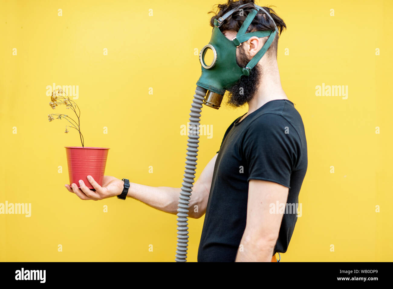 Portrait of a sad man with gas mask and dried flowerpot on the yellow ...