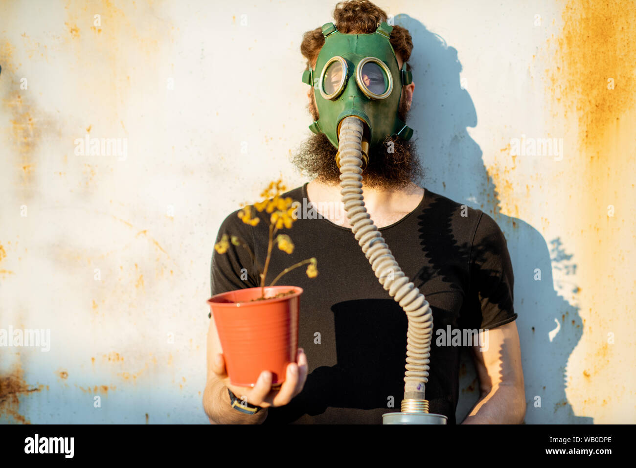 Portrait of a sad man with gas mask holding dried flowerpot on the grey ...