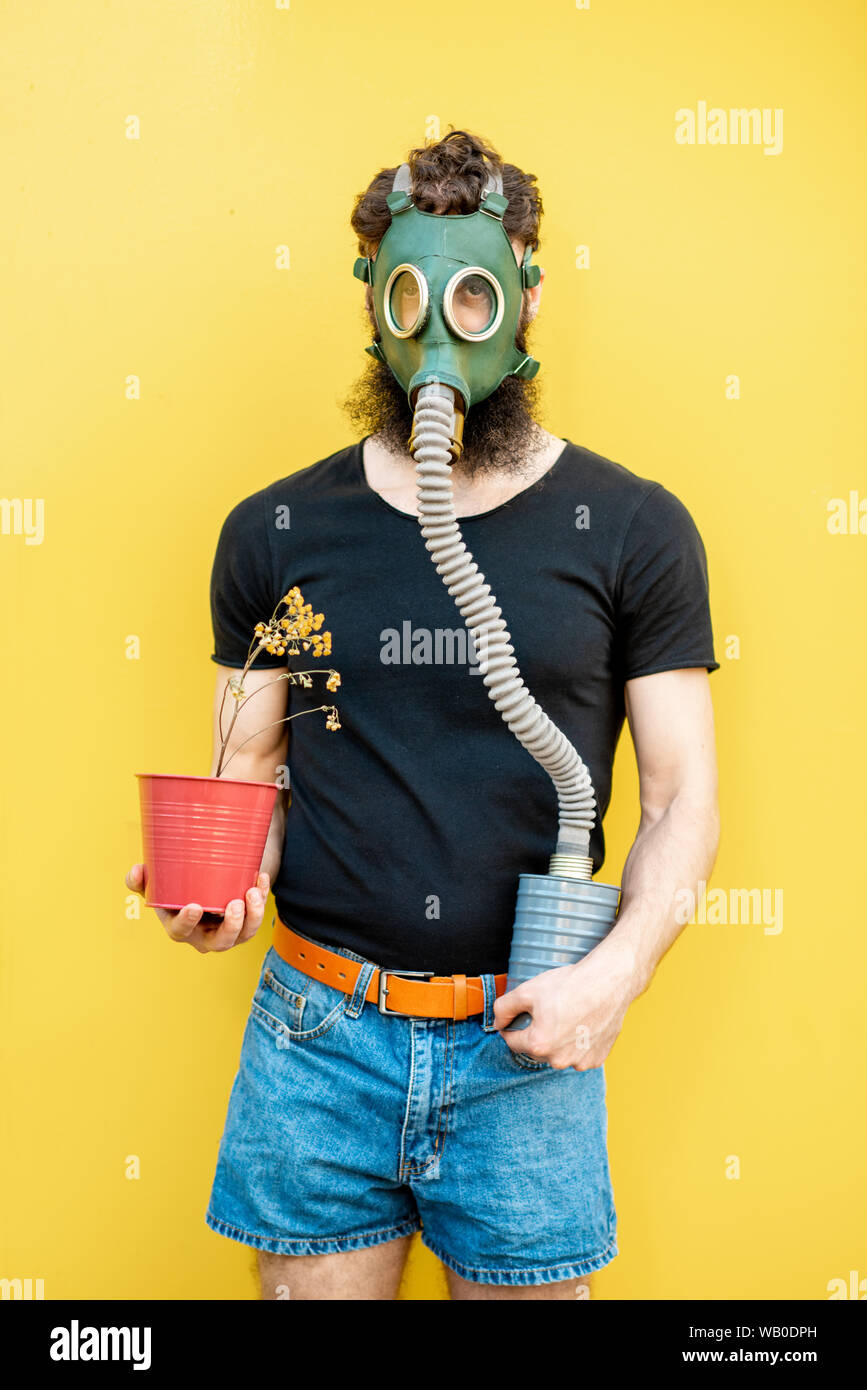 Portrait of a sad man with gas mask and dried flowerpot on the yellow ...