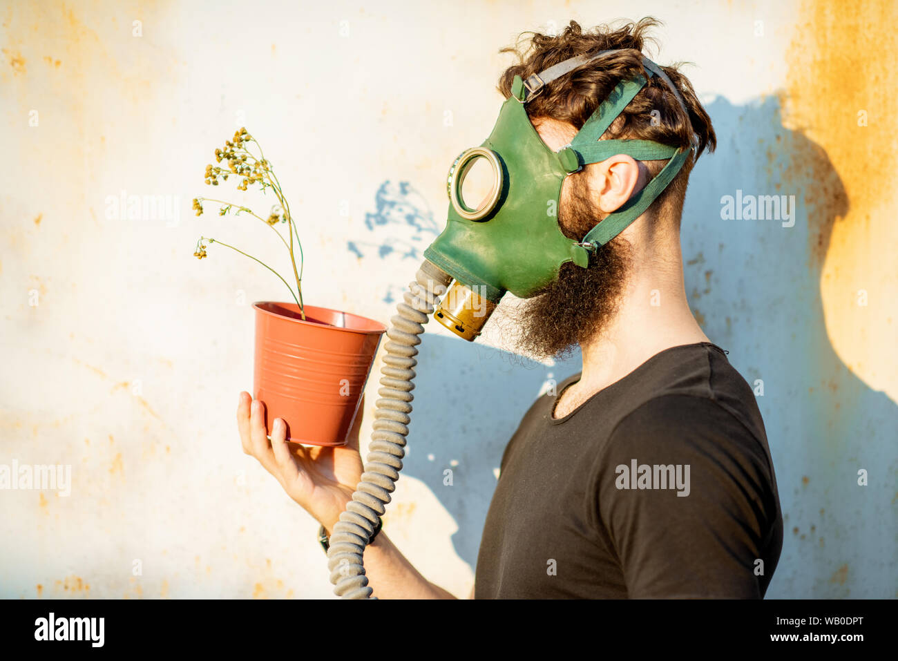 Portrait of a sad man with gas mask holding dried flowerpot on the grey ...