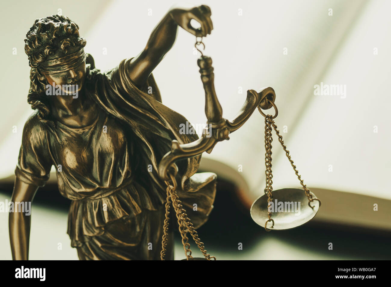 Silver figure of Justice holding scales and a sword against an open law ...