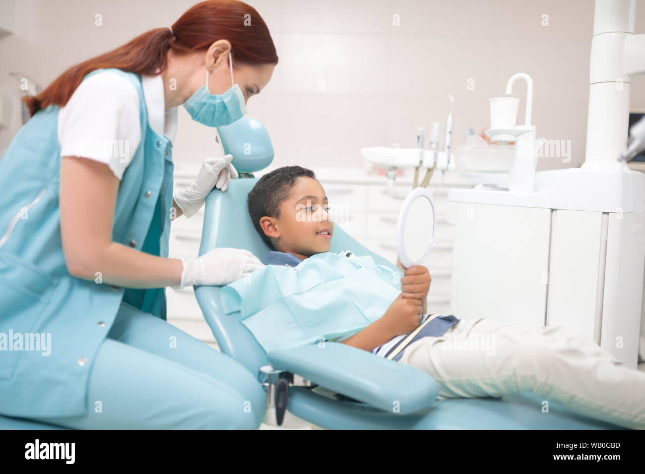 Red-haired dentist wearing mask giving mirror to boy Stock Photo - Alamy