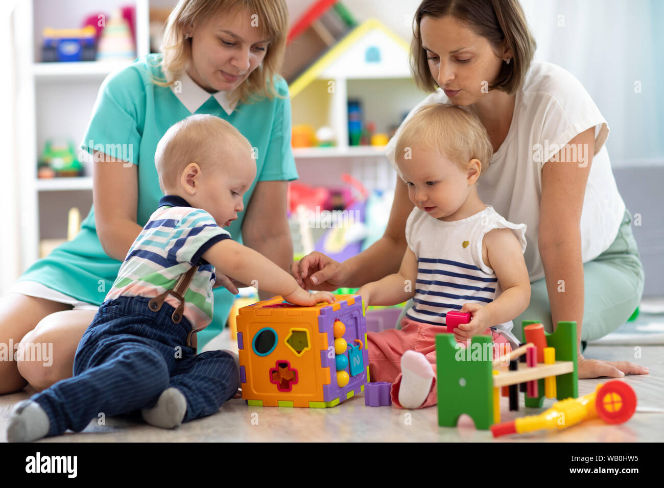 Group of babies play together with mothers in the classroom in nursery ...
