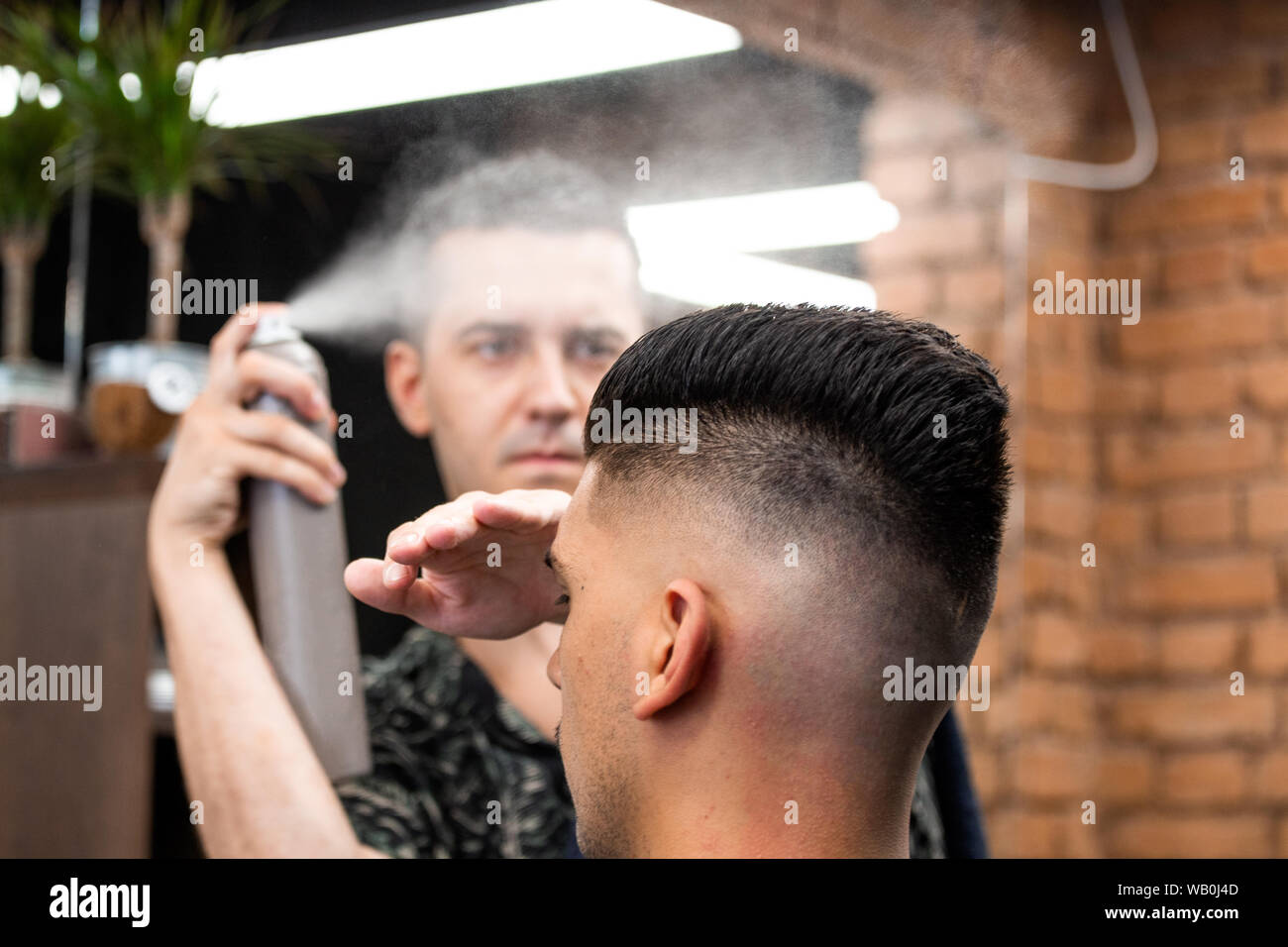 Professional Hairdresser using hair spray on client hair at barber shop ...