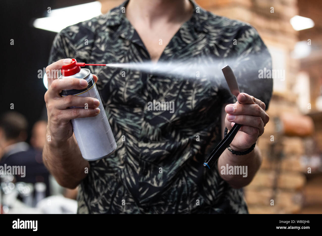 Master disinfecting shaving instrument before use. Young man spray ...