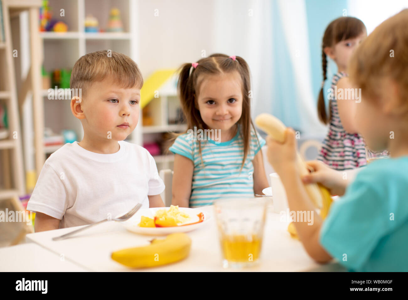 Kids have a lunch in daycare centre. Children eating fresh fruits in ...