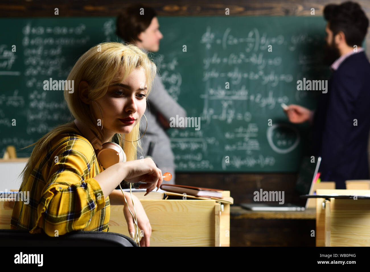 Confident student studying for exam at desk with laptop reading a book ...