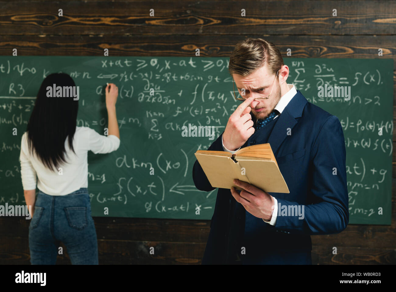 Female student solving equation at the board. Young teacher with short ...