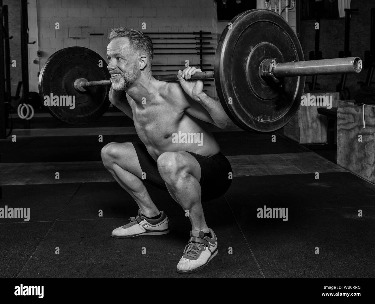 A fit older man with Sixpack is doing back squats with the barbell ...