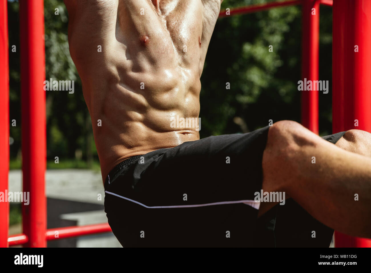 Young muscular shirtless caucasian man doing crunches on horizontal bar ...