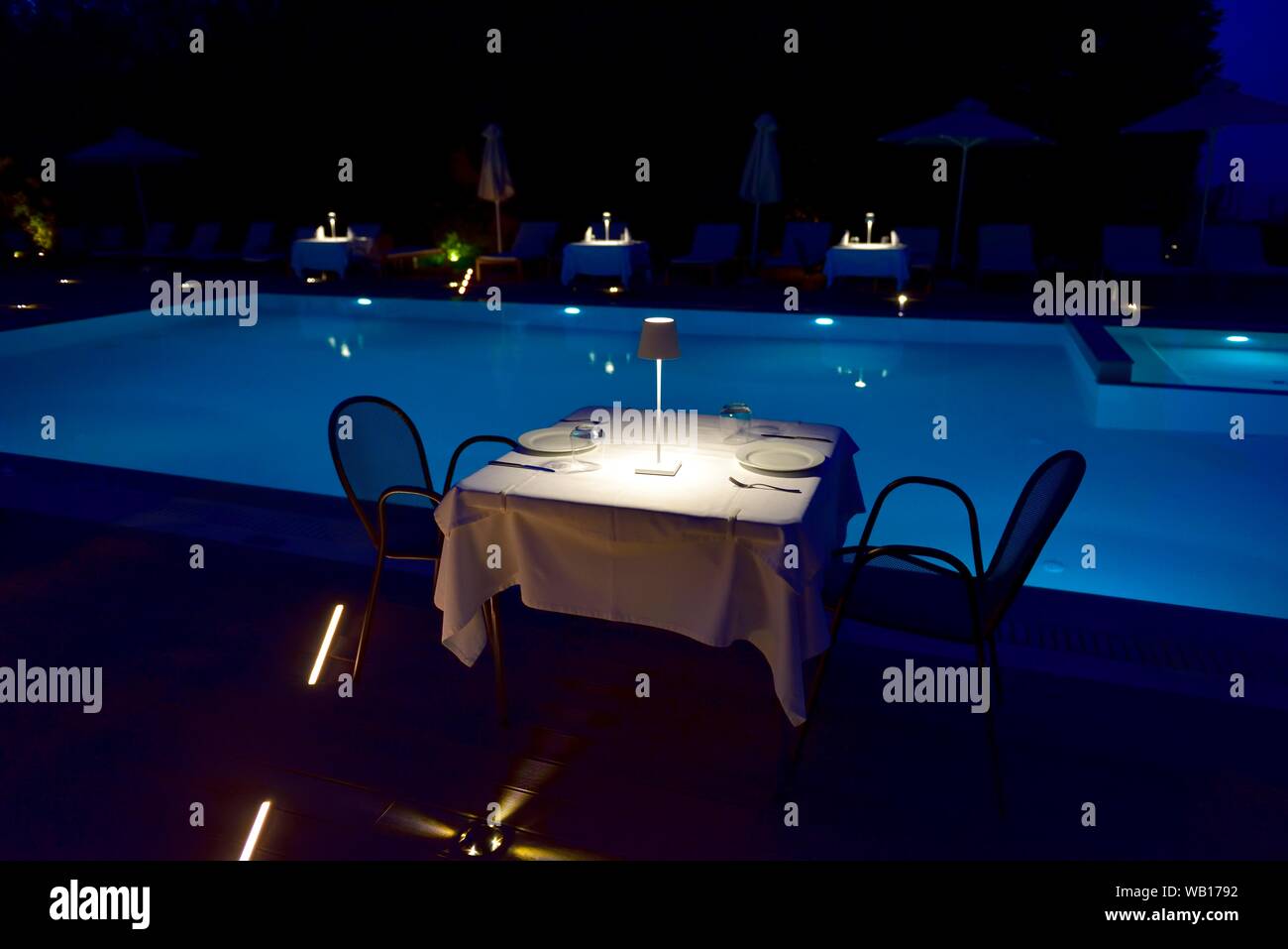 Romantic dinner tables set for two,at the side of a hotel swimming pool ...