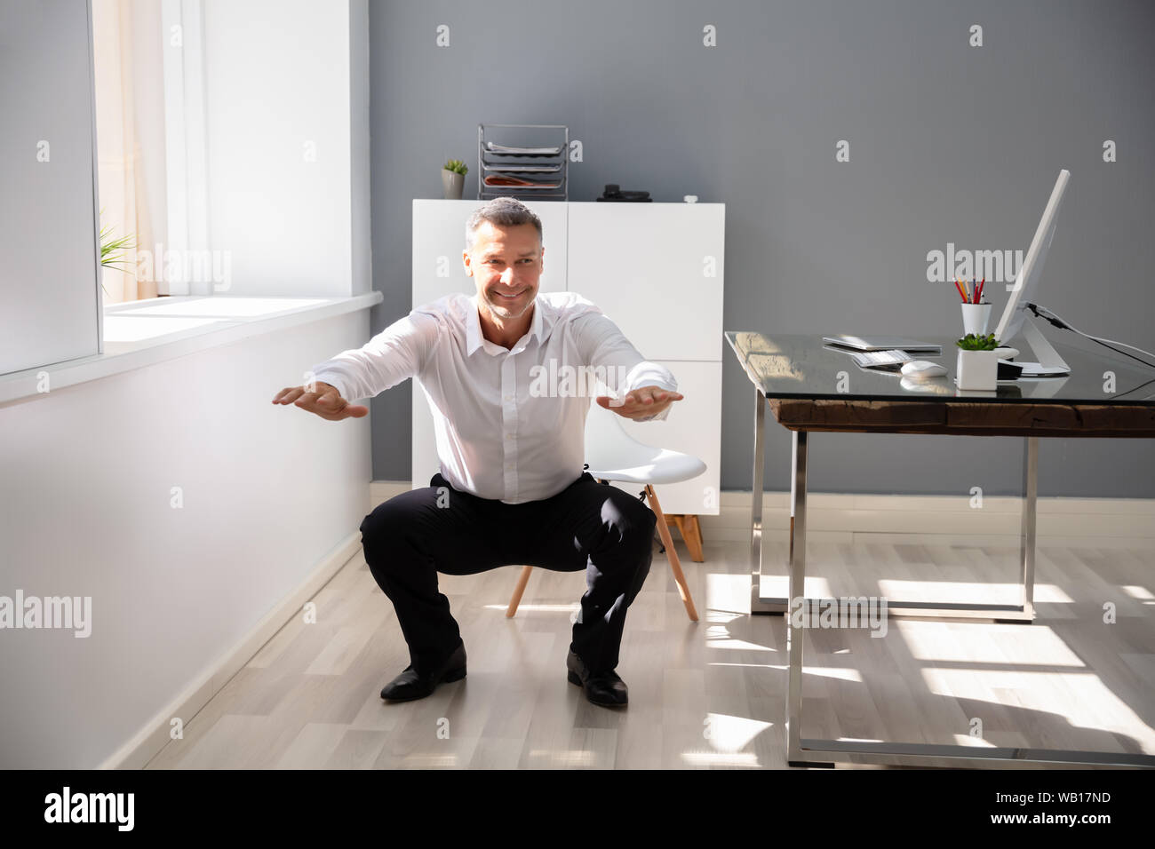 Happy Businessman Doing Squats Exercise In Front Of Computer At Office ...