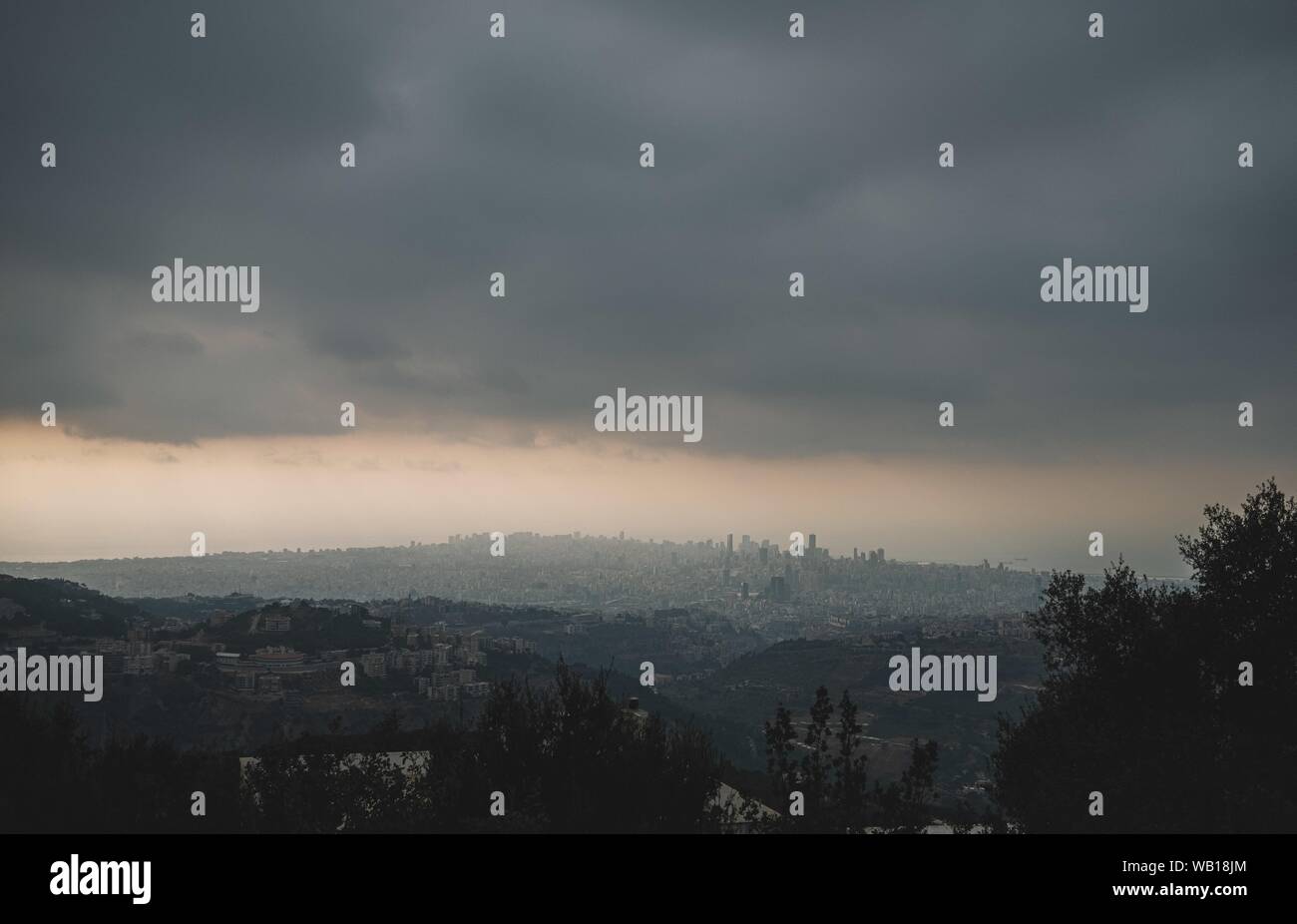 Wide shot of city surrounded with trees and mountains under a dusky sky ...