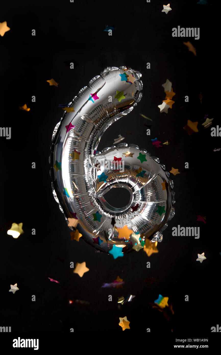 Silver balloon and confetti for 6th birthday in front of black ...