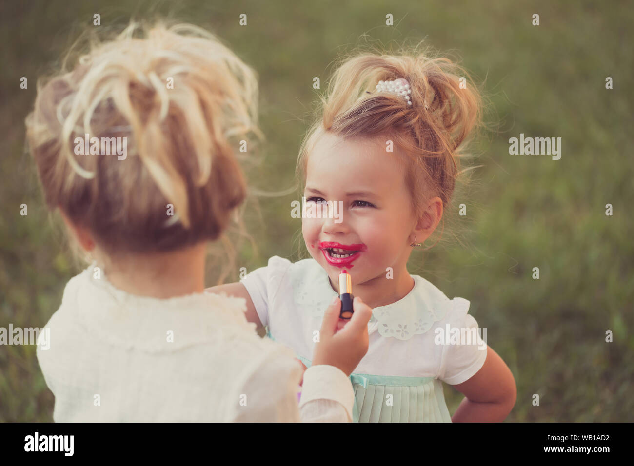 Girl do makeup for sister on green grass background. Baby apply red ...