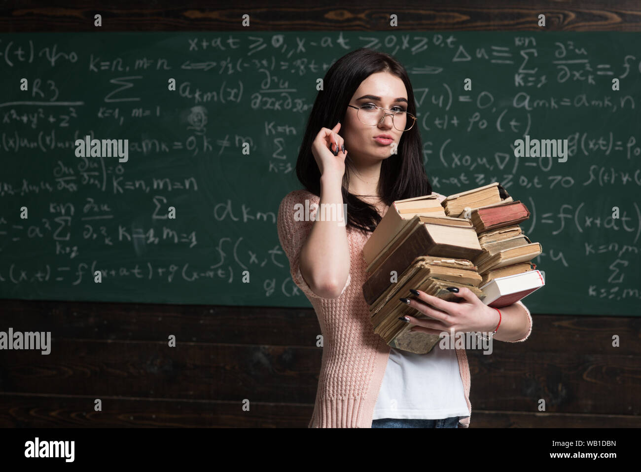 Course project. Girl holds heavy pile of old books, chalkboard ...