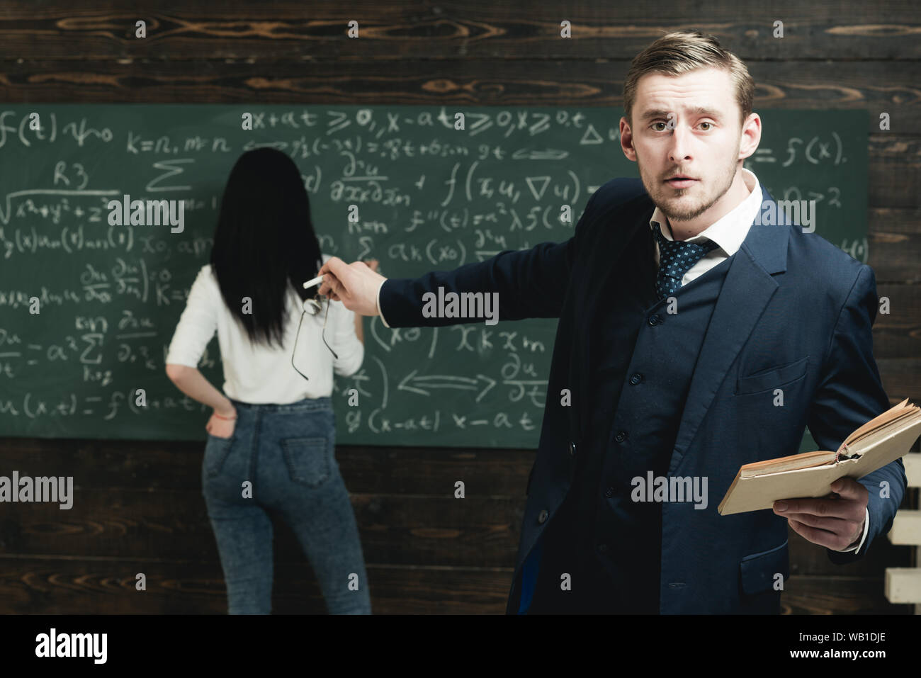 Agitated young professor pointing at green board with a lot of writing ...