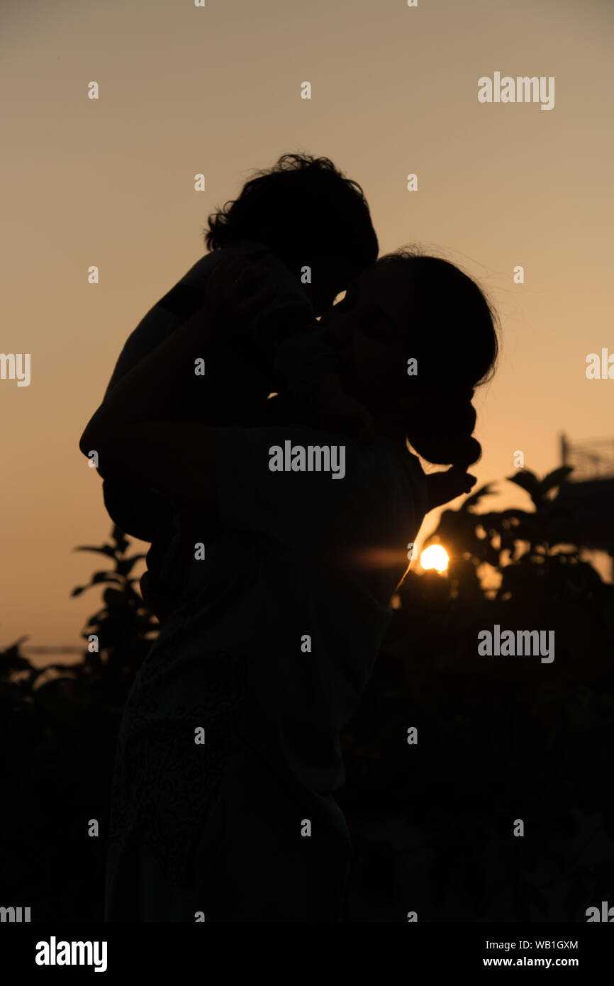 A silhouette of a happy young girl child the arms of his loving mother for a hug, in front of ...