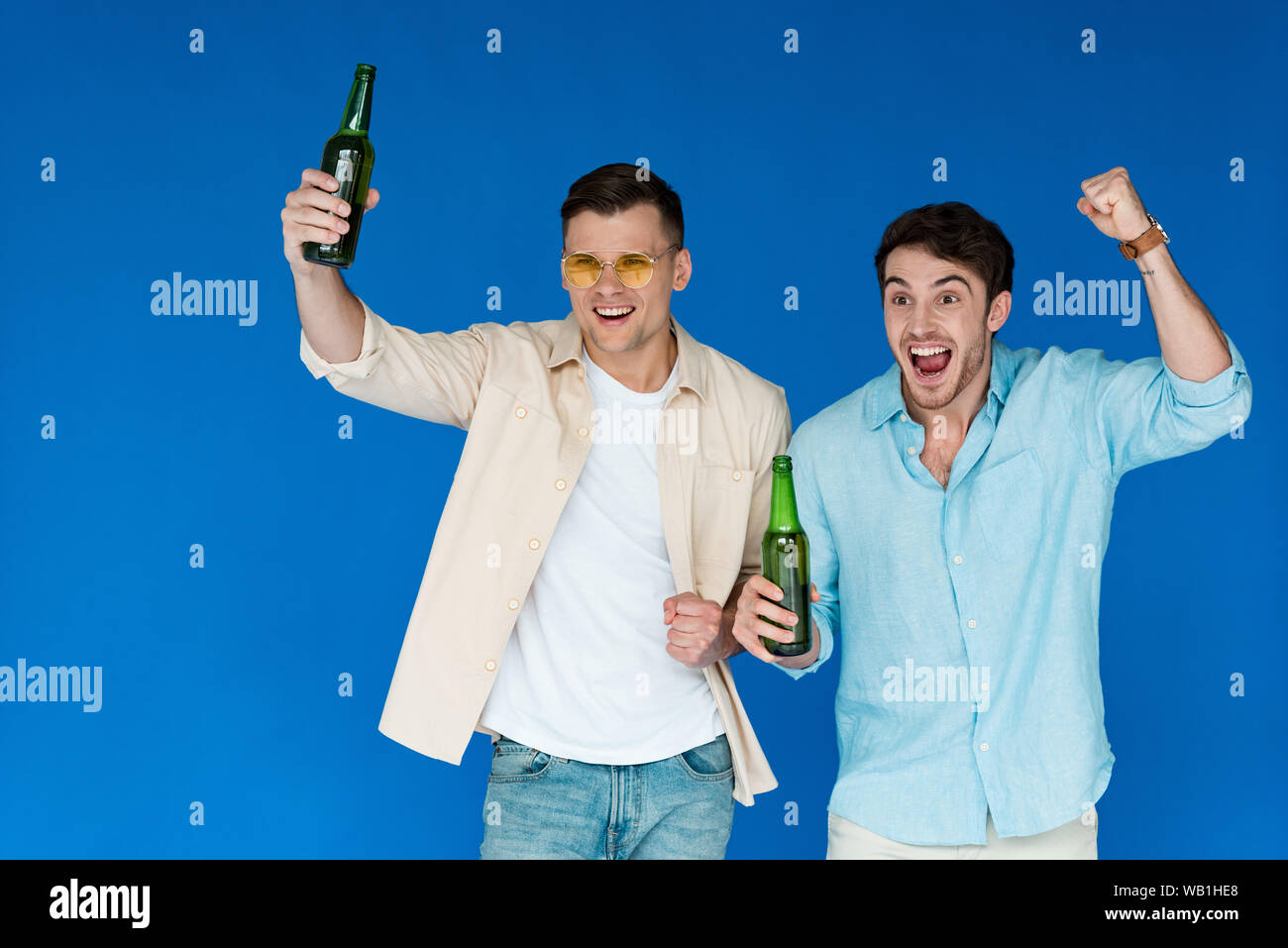 two excited friends holding bottles of beer and showing yes gesture ...