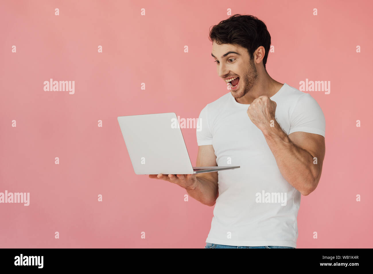 excited muscular man in white t-shirt using laptop and showing yes ...