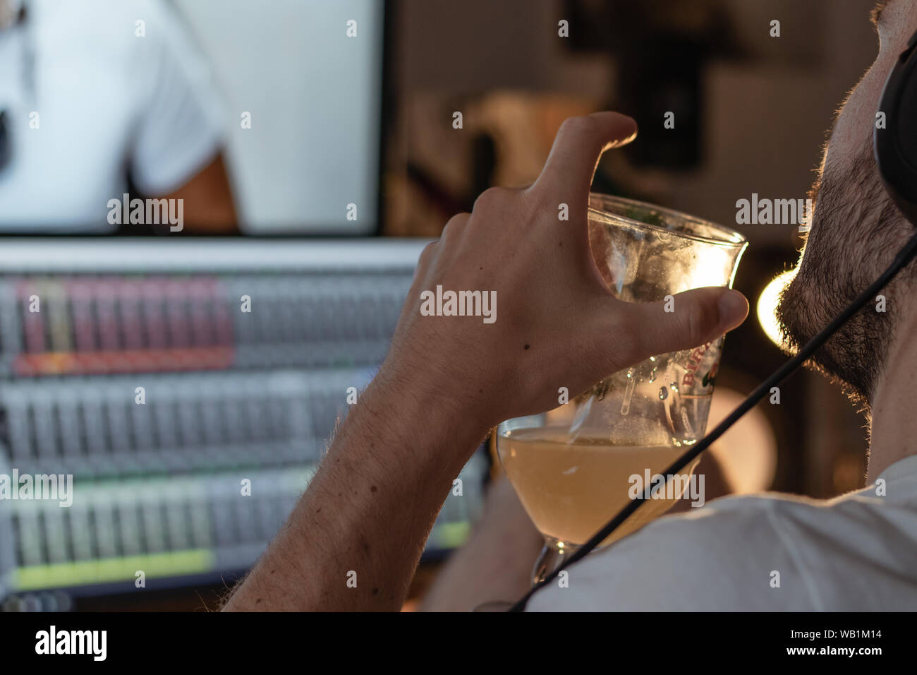 boy doing sound mixing in a studio in low light while he drinks a beer ...