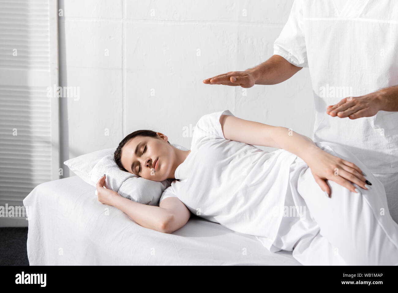 cropped view of healer standing near sleeping woman and holding hands ...